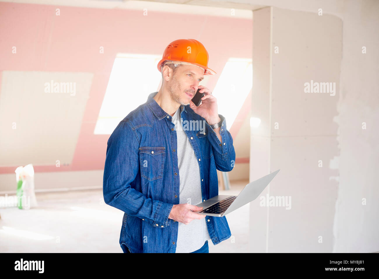 Construction man making call and using his laptop while standing at ...