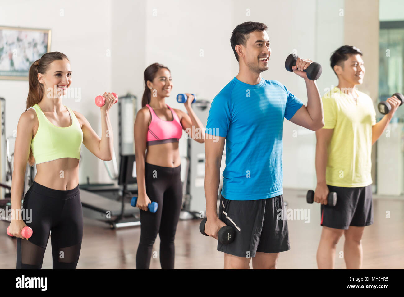 Fit handsome man smiling while exercising bicep curls during group ...