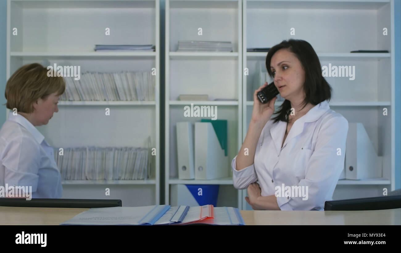 Smiling female nurse answering phone at the hospital reception desk ...