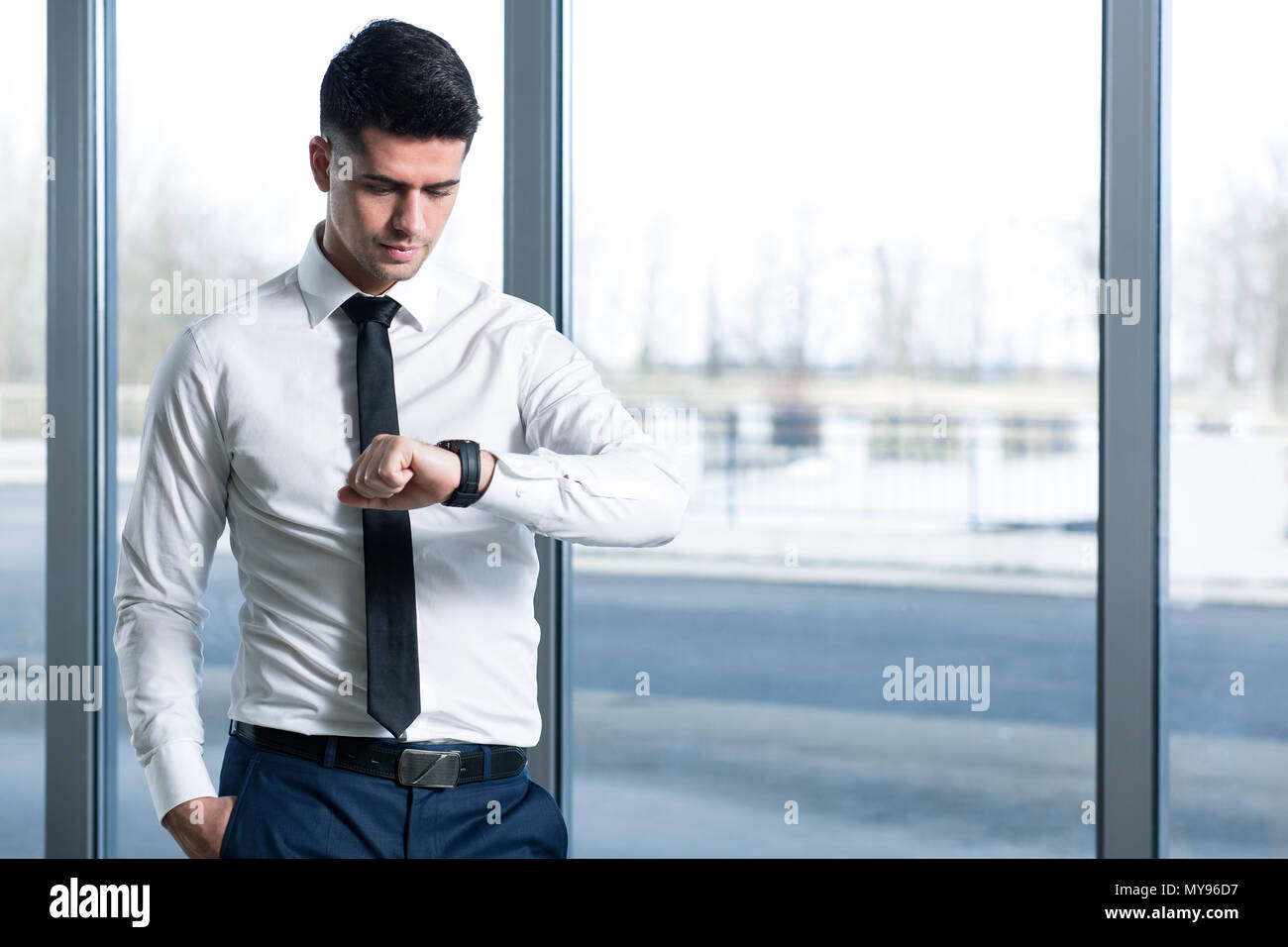 Elegant businessman looking on his wristwatch, standing in modern ...