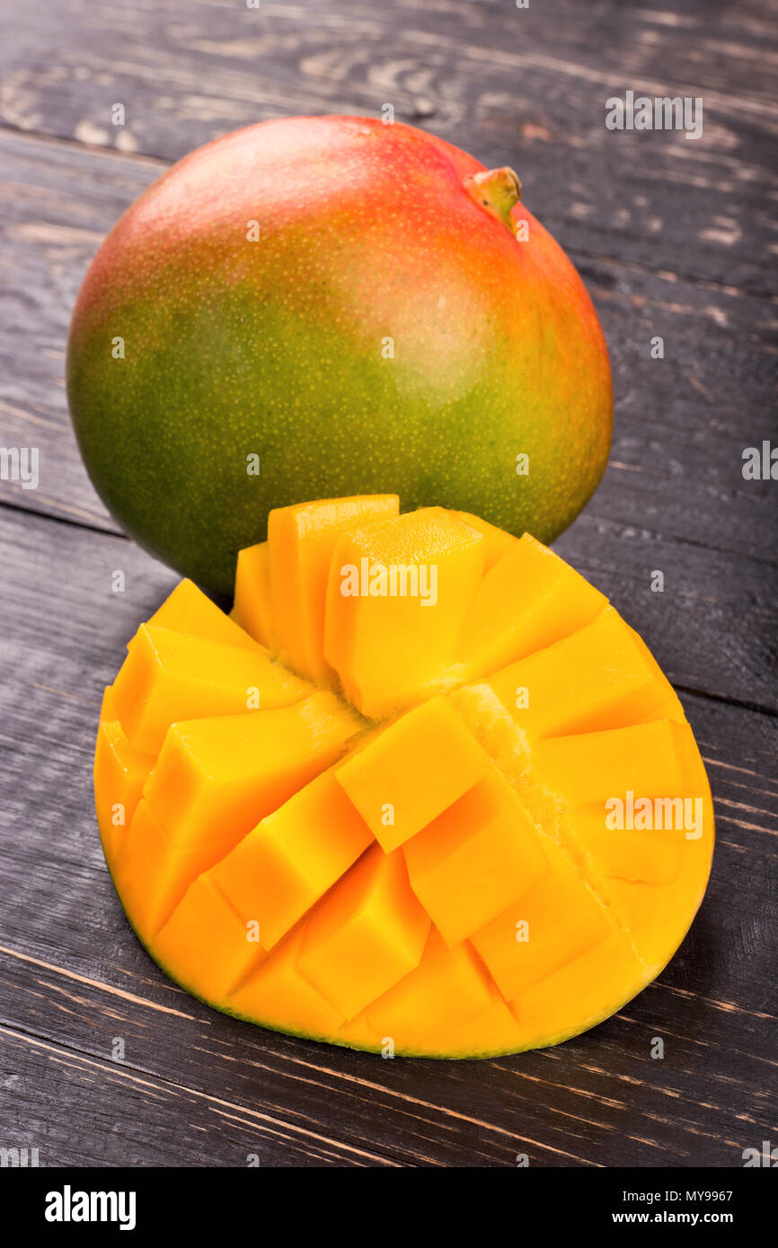Fresh mango fruit with half cut into pieces on the dark table closeup ...