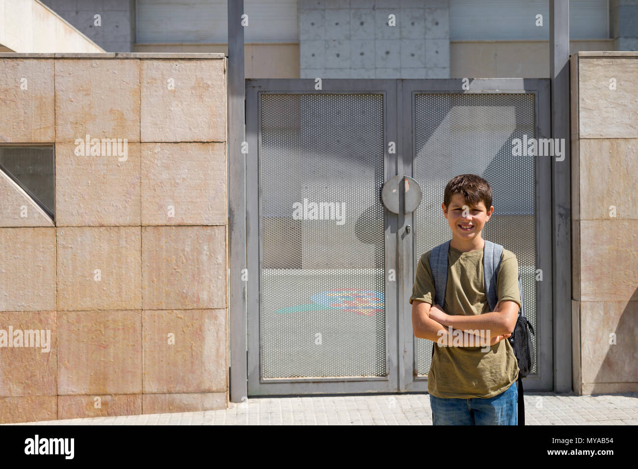 Cheerful child carrying his backpack standing in front of the school ...