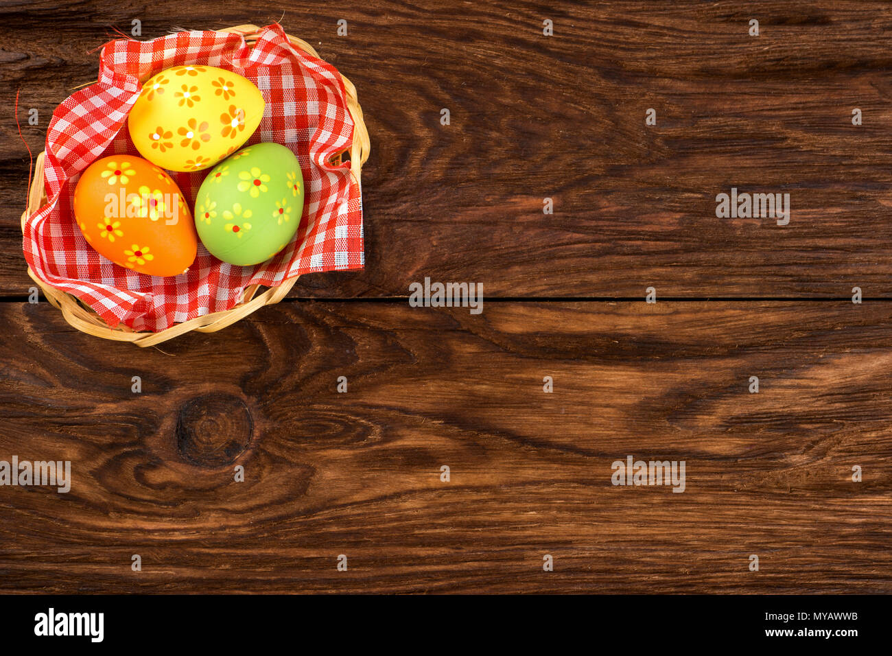 Three Easter eggs in a basket on an empty wooden background a top view ...