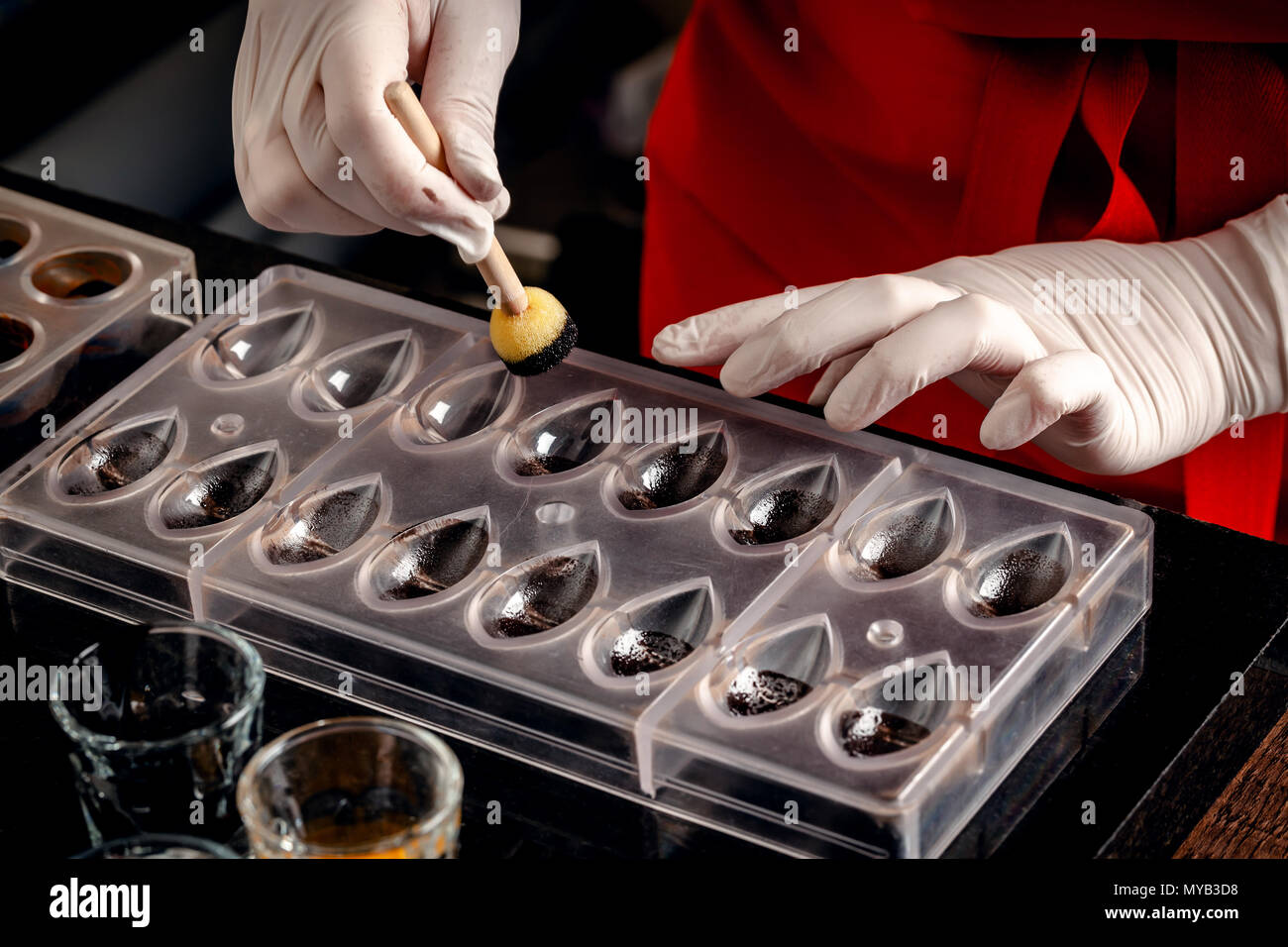 A woman confectioner with red uniform and white sterile gloves do a set ...