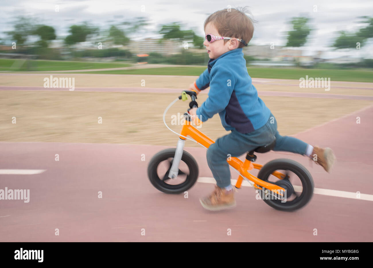 Boy in blue jacket riding fast an orange balance bike or run bike ...