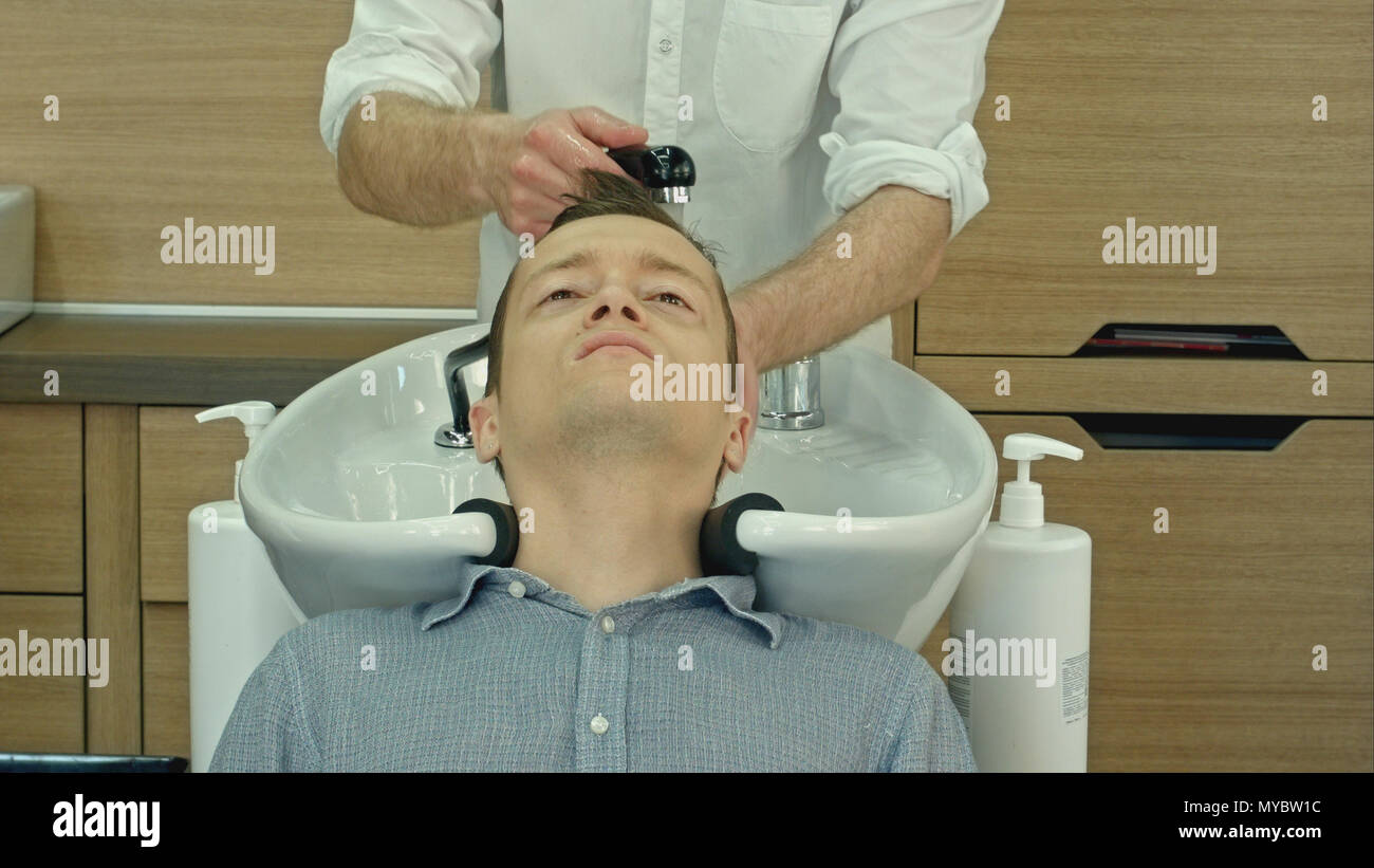Handsome man having his hair washed in hairdressing saloon. Young man ...