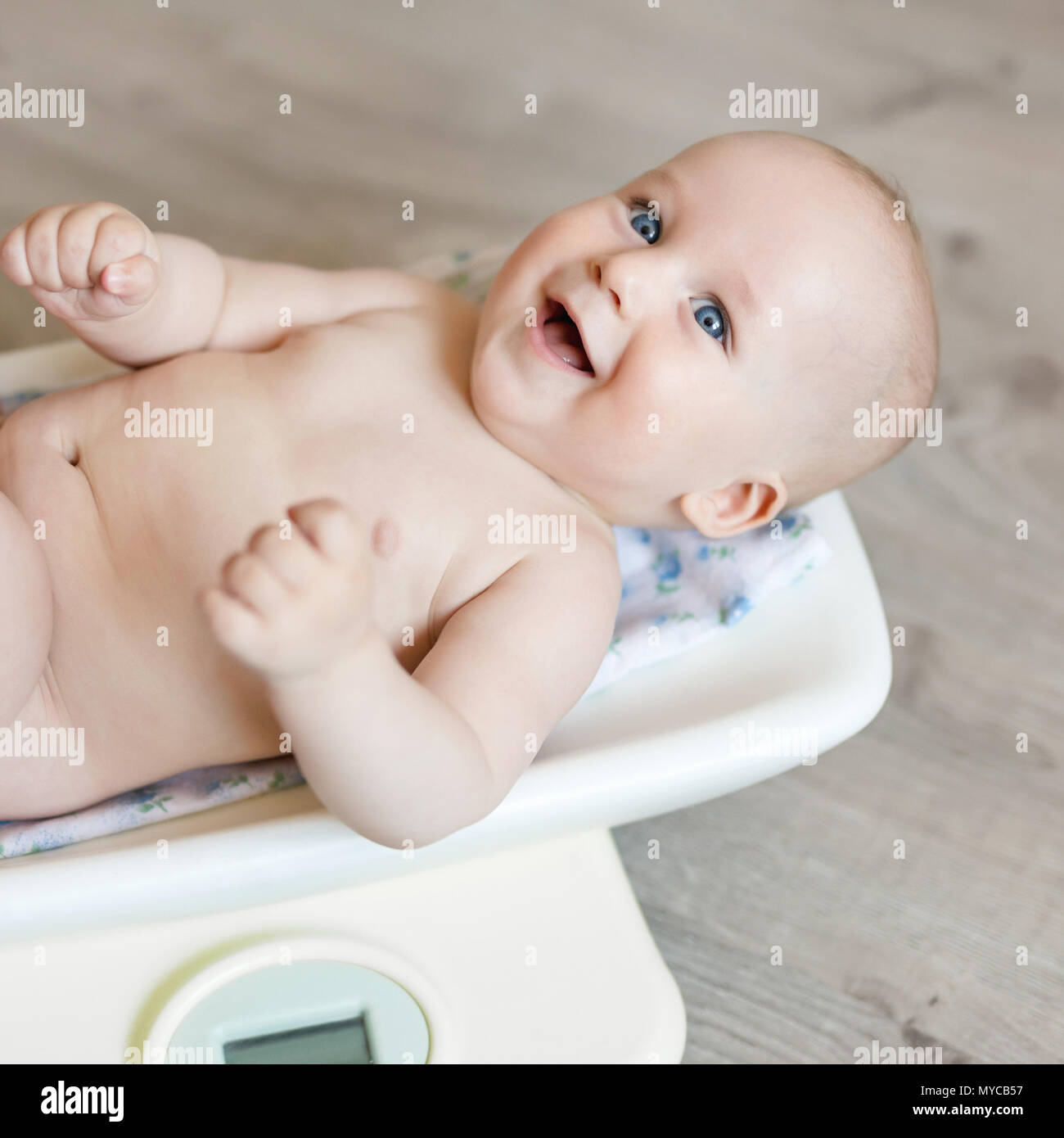 Scales with cute laughing baby on wooden surface at home. Measuring ...