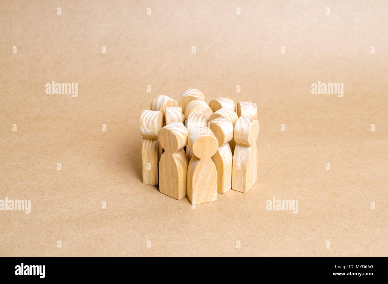 A crowd of wooden figures of people stands in a pile on a beige paper ...