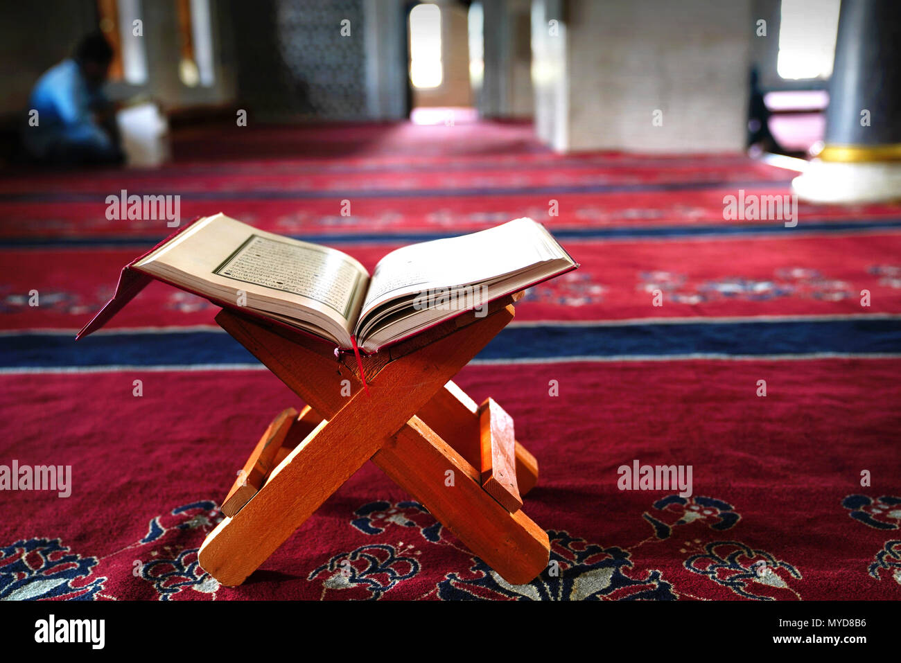 Holy Koran on stand on red carpet and blurred interior of a mosque in ...