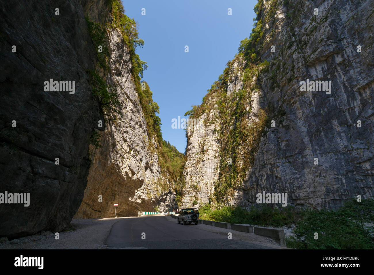 Road along the bottom of a deep canyon. An off-road car is parked at ...