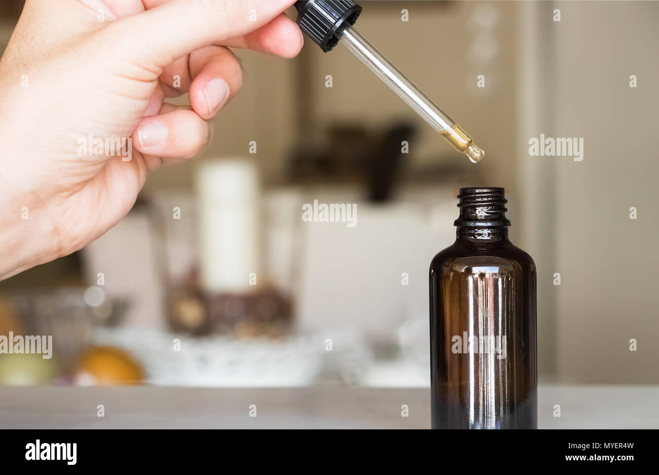 Male hand holding a glass dropper above a brown bottle, indoors ...