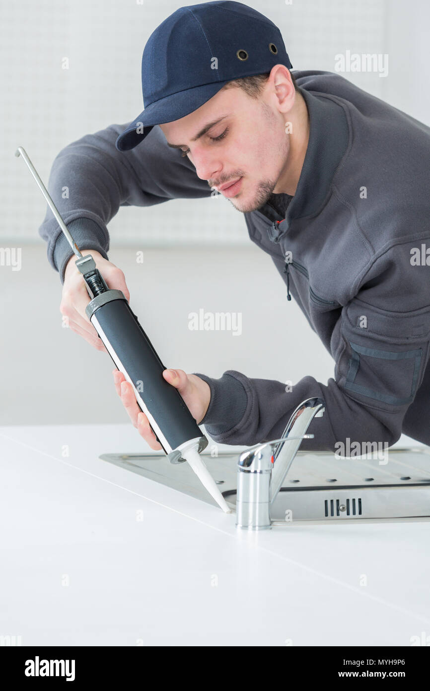 young handyman applying silicone sealant with gun around sink Stock ...