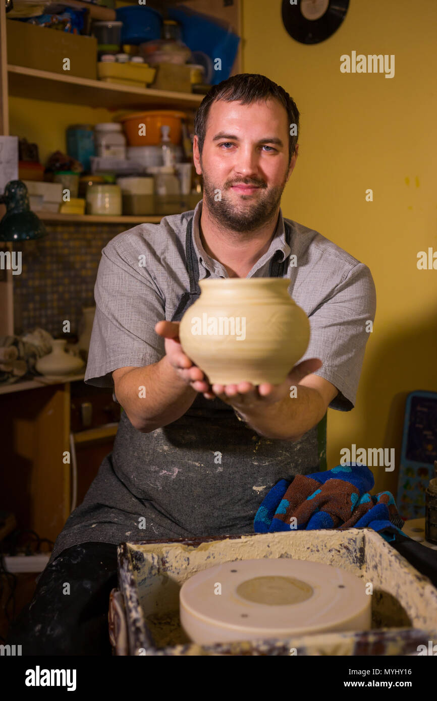 Professional male potter showing earthenware pot in pottery workshop ...