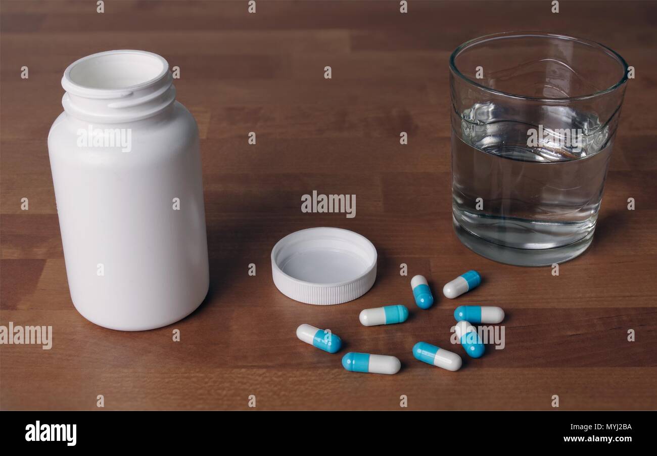 Open pill bottle with blue capsules beside a glas water Stock Photo - Alamy