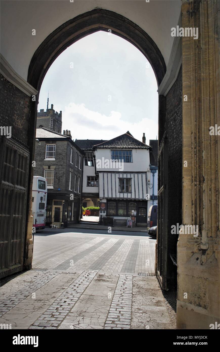 view out of the entrance gate arch of Norwich cathedral to wonky tudor ...