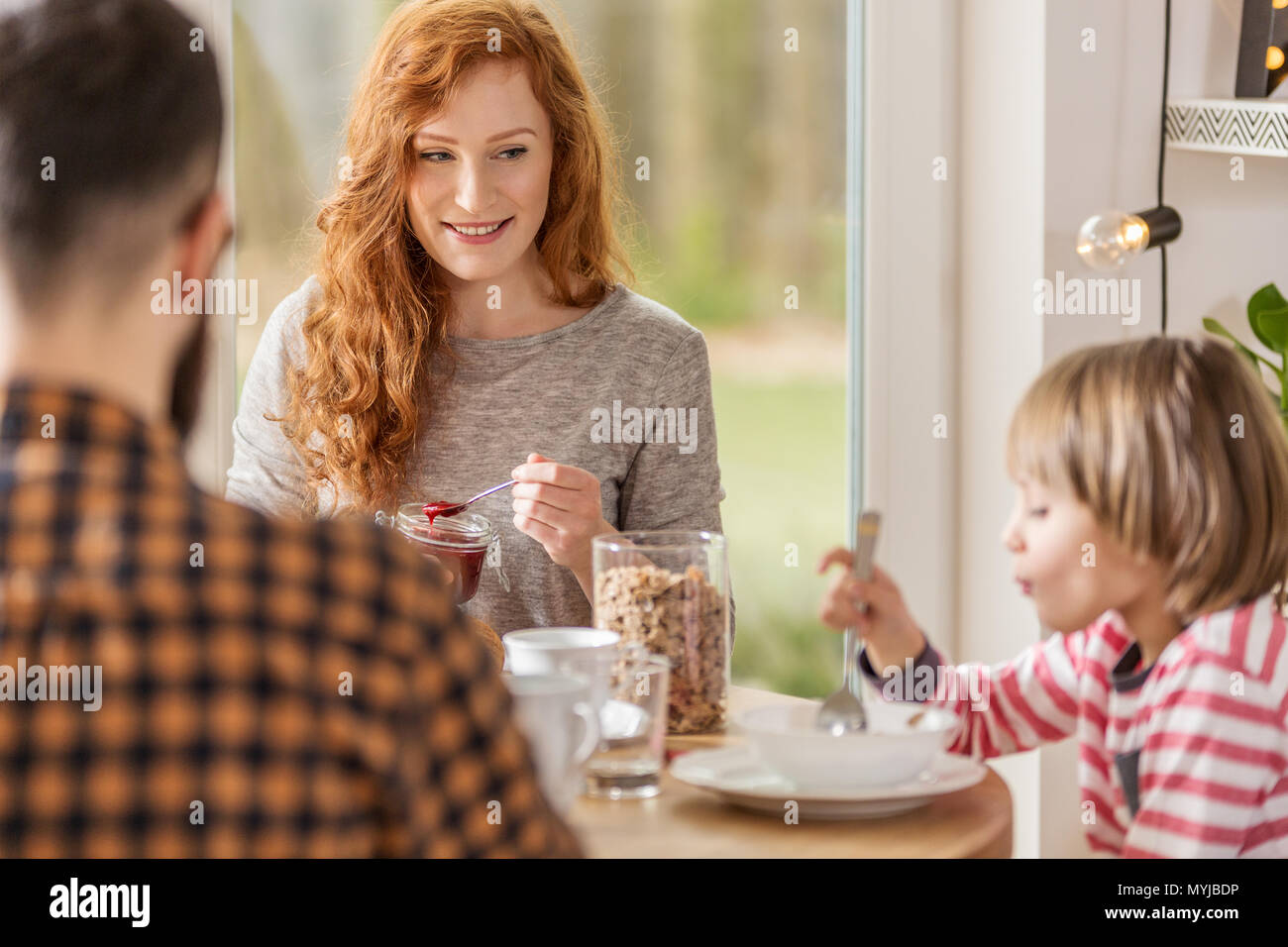 Young family eating breakfast together in a living room with big window ...
