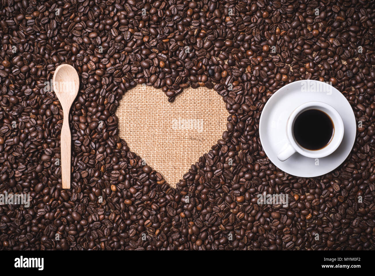 top view heart shape coffee beans on juta textile with wood tea spoon ...