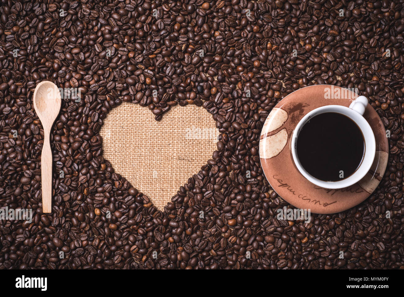 top view heart shape coffee beans on juta textile with wood tea spoon ...