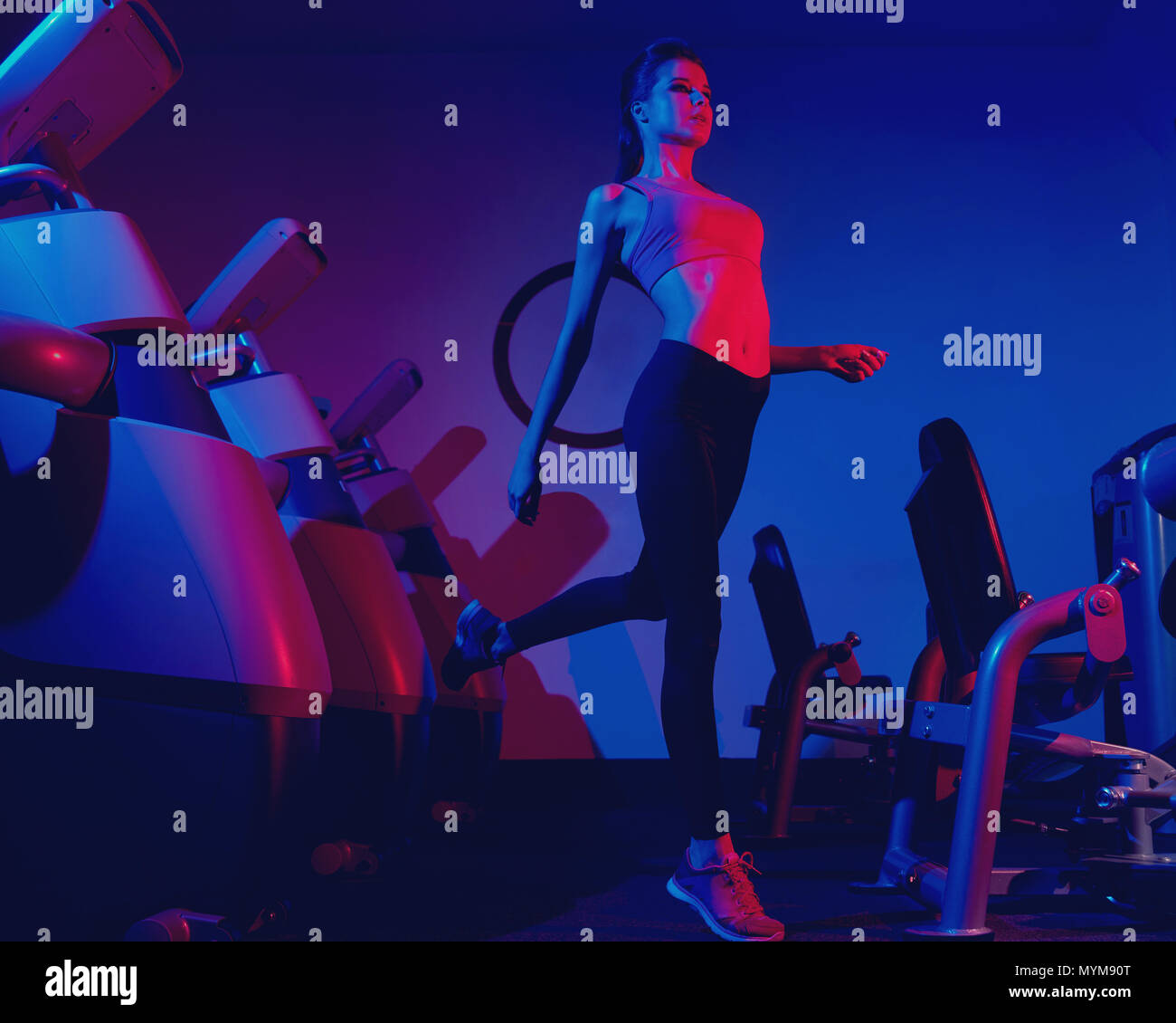 Slim woman jumping between rows of exercise machines Stock Photo - Alamy