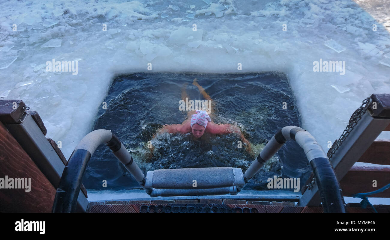 Person emerging from a swimming hole cut in the frozen ice surface of a ...