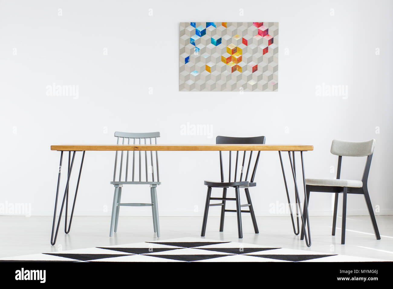 Colorful poster on white wall in dining room with geometric carpet and ...