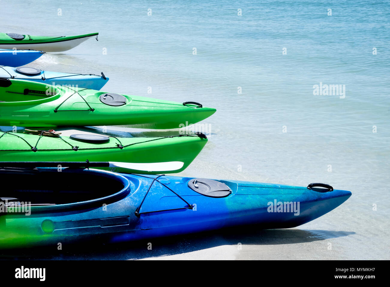 six canoes three blue and three green on the edge of a sandy beach sea ...