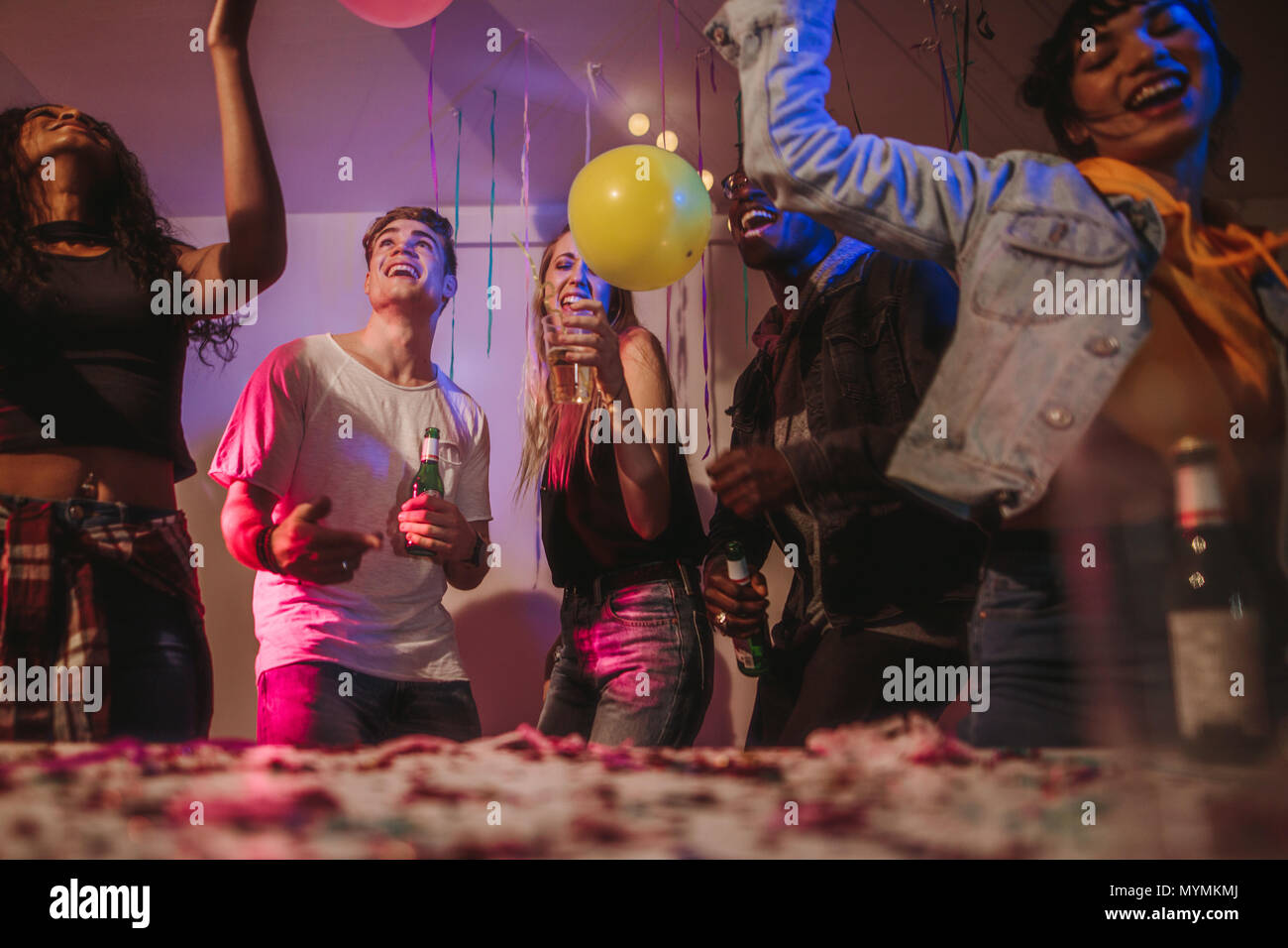 Young men and women having fun at a colorful house party with ...