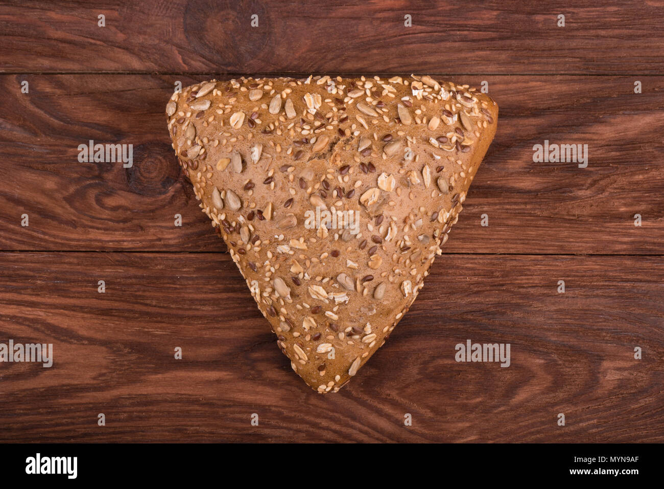 Triangular bun with different grains on a brown wooden background a top ...