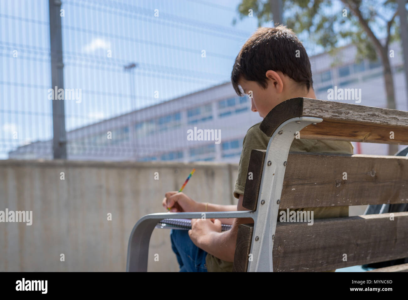 Portrait of a teenager boy sitting on a wood park bench doing his ...