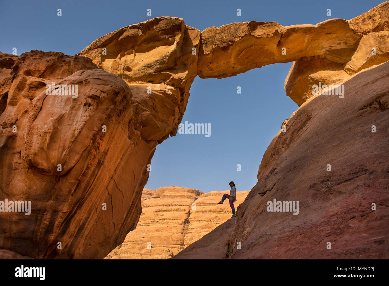 Tourist posing under the Um Fruth rock bridge in Wadi Rum desert ...