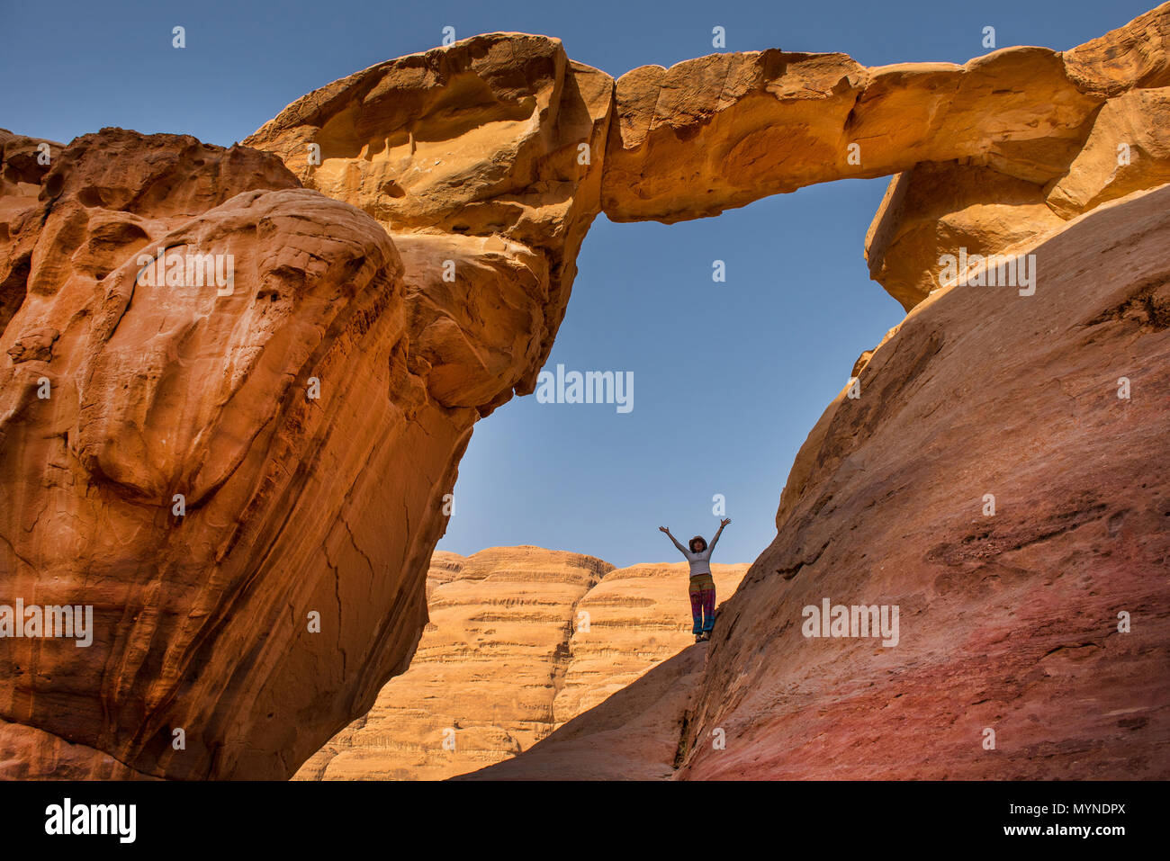 Tourist posing under the Um Fruth rock bridge in Wadi Rum desert ...