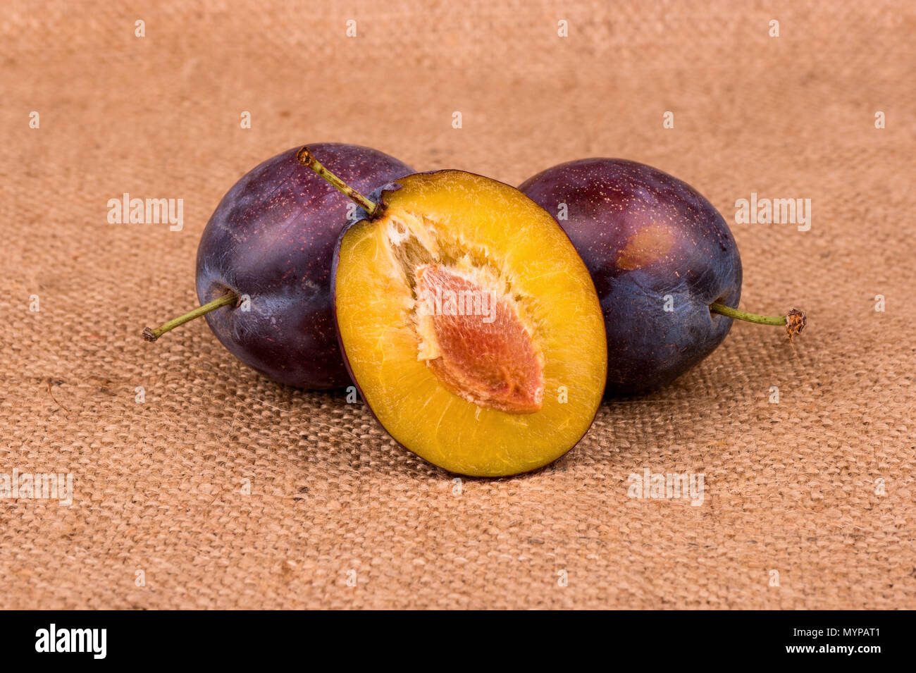 Two fresh plums with cut half on sacking Stock Photo - Alamy