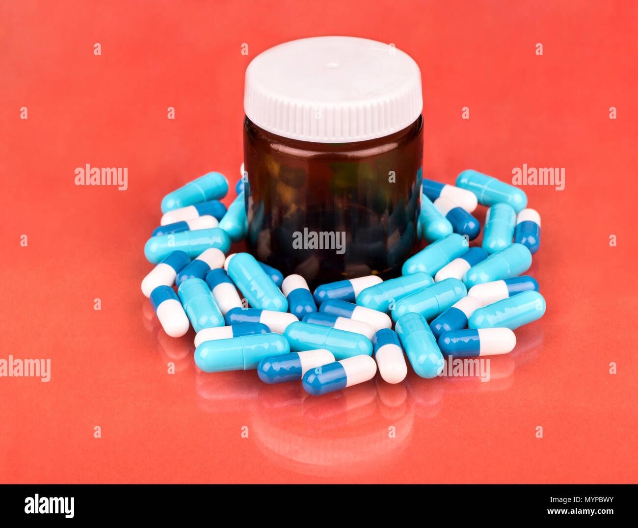 Multi-colored capsules lay near empty bottle on a peach background ...