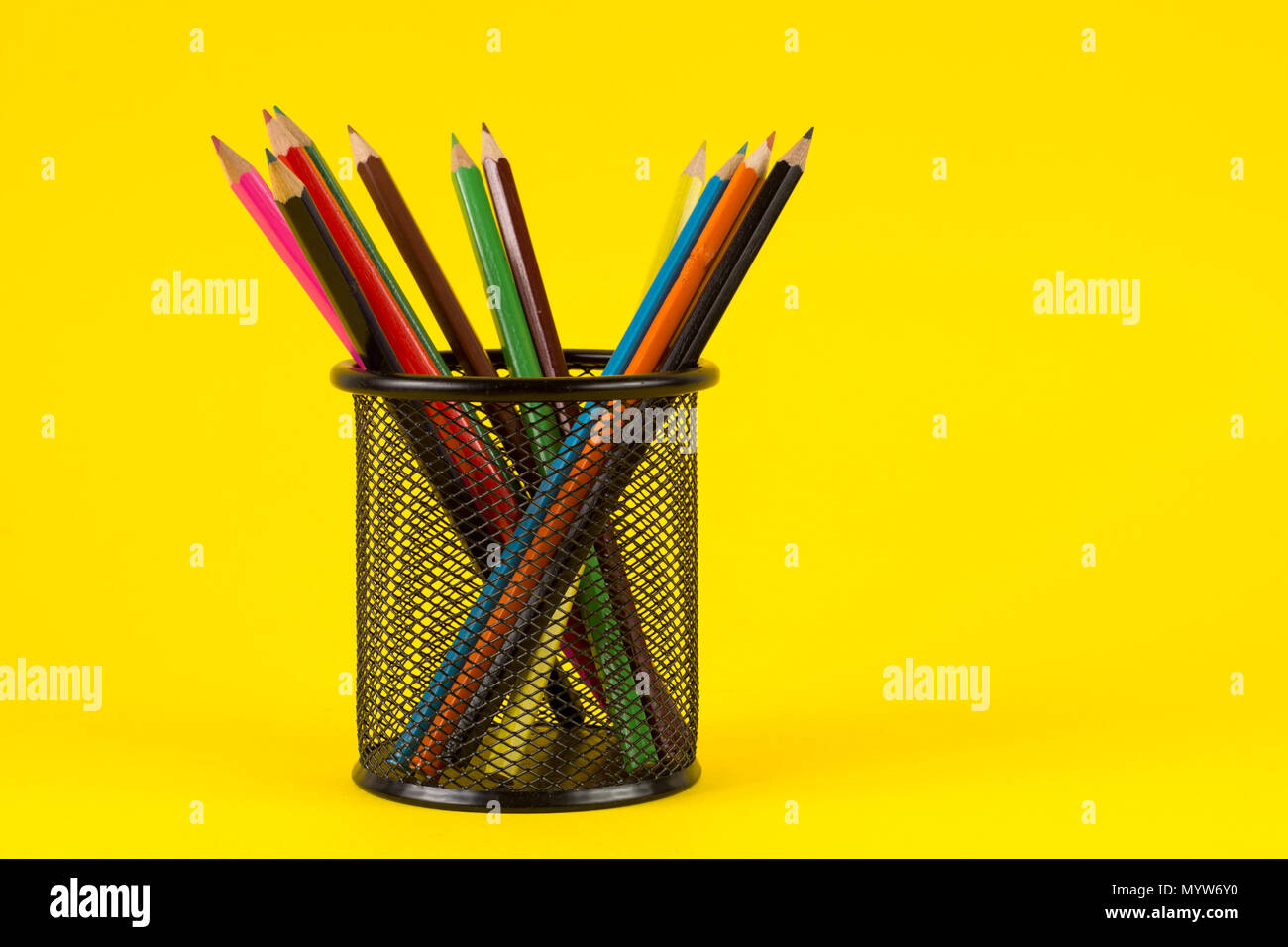 Colored wooden pencil in black metal basket isolated on yellow ...