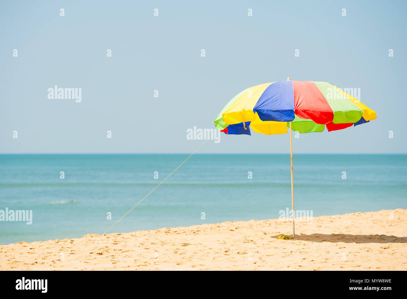 A colorful umbrella is open on a tropical beach during a sunny day ...