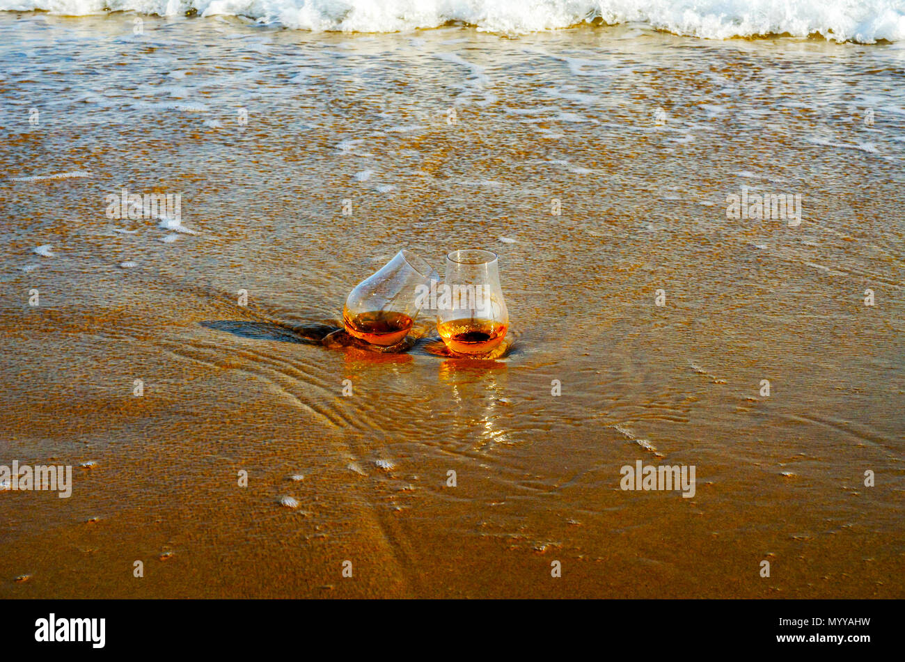 glass of whiskey single malt on the sand washed by the waves, a glass ...