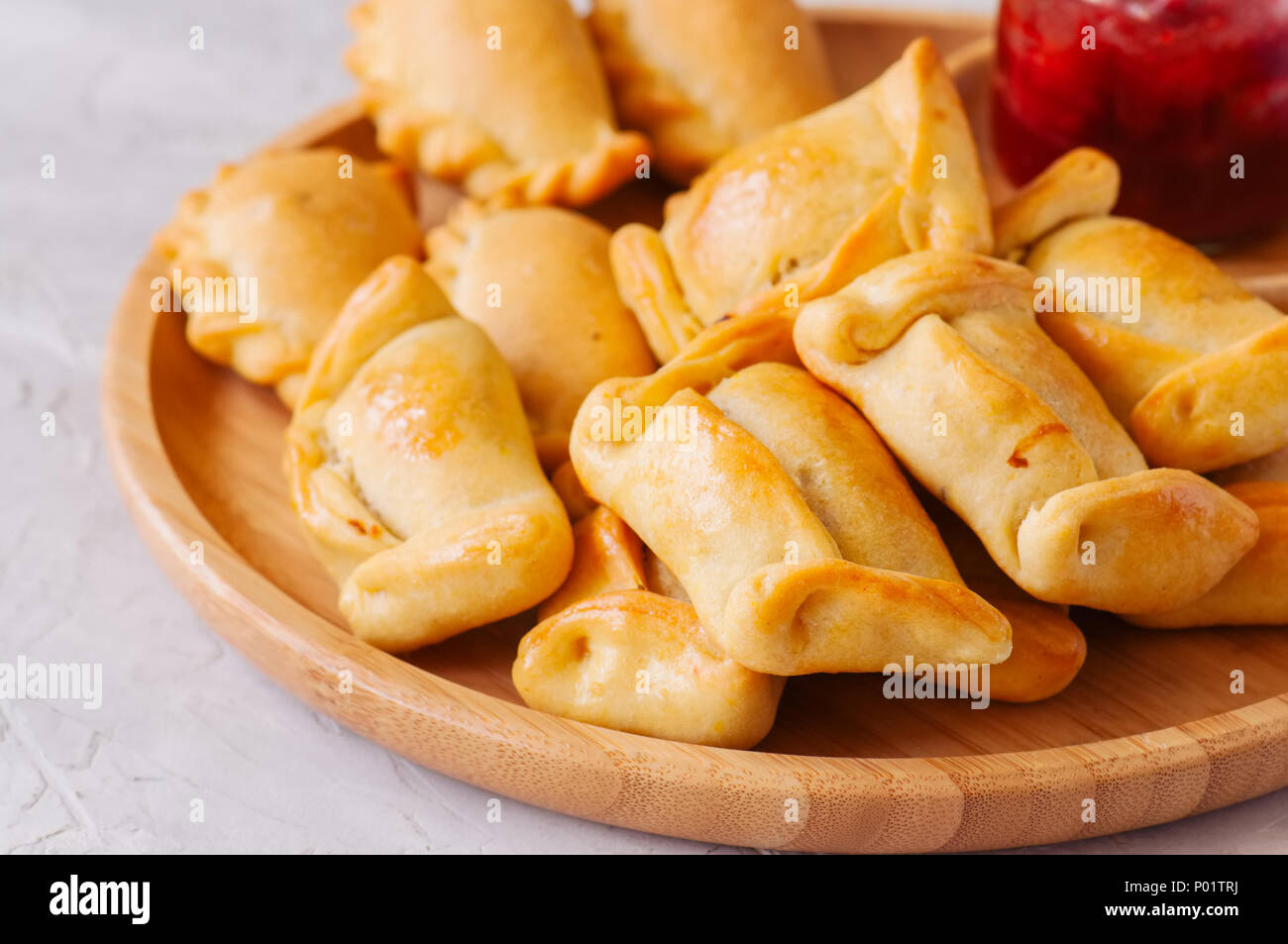 Two types of empanadas on a wooden plate with ketchup. White stone ...