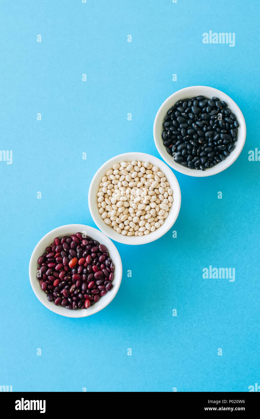 Tree types of dried beans in a white bowls on a light blue background ...