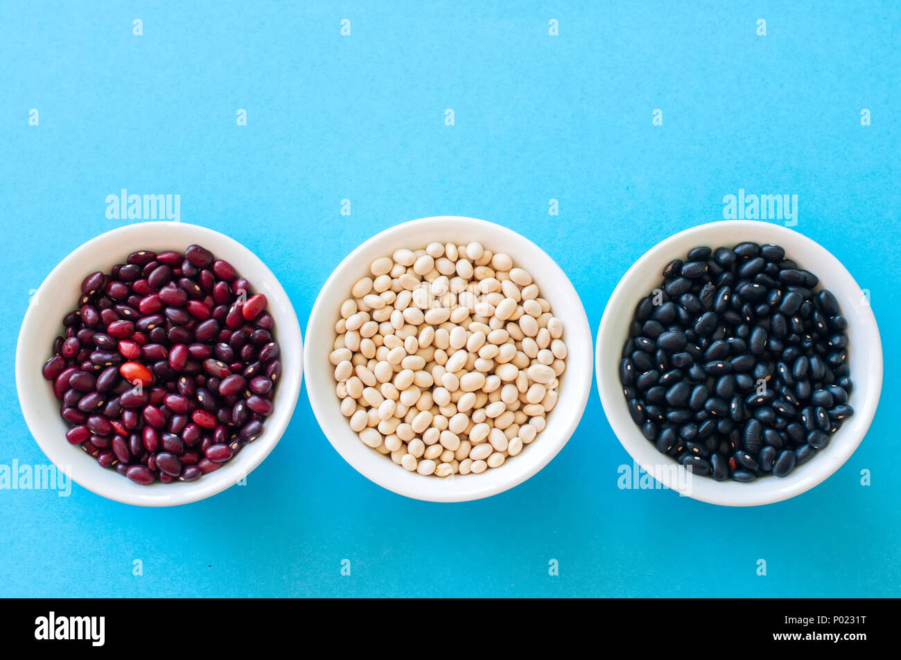 Tree types of dried beans in a white bowls on a light blue background ...
