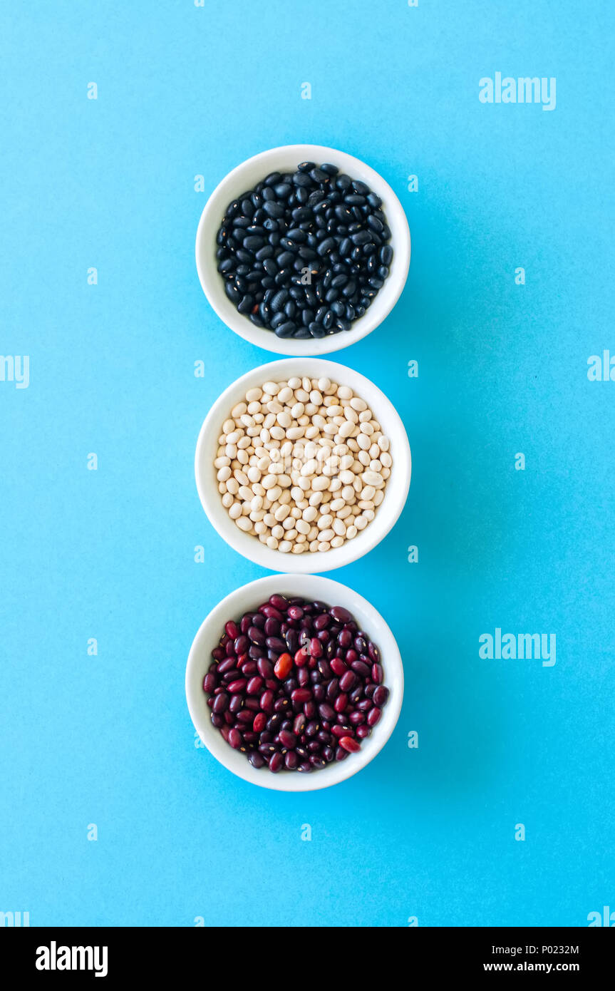 Tree types of dried beans in a white bowls on a light blue background ...