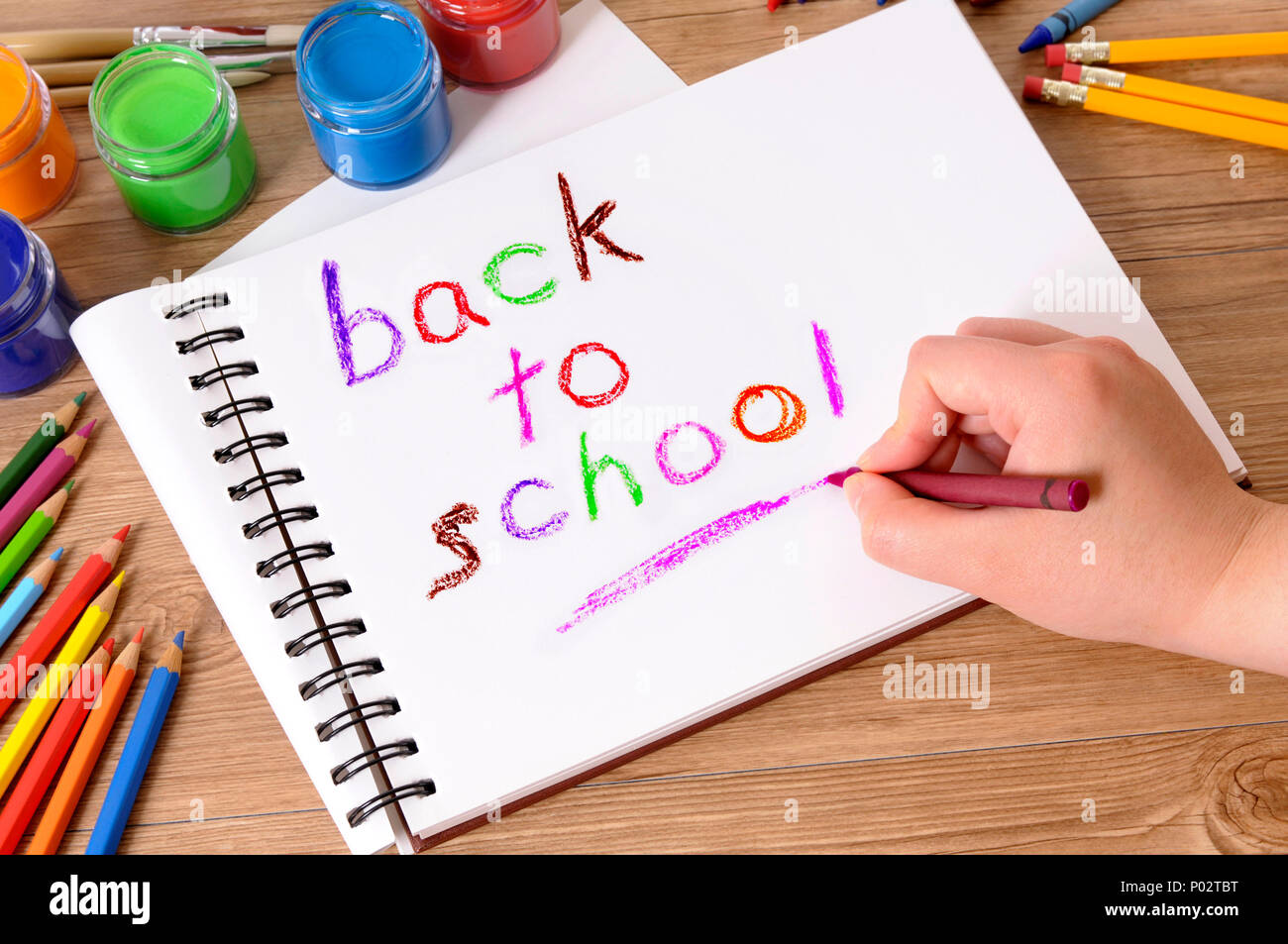 Child writing the words Back to School on a white folded notebook with ...