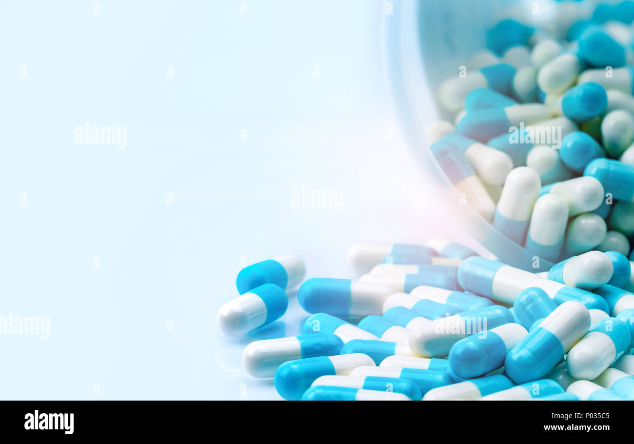 Blue and white capsules pill spilled out from white plastic bottle ...