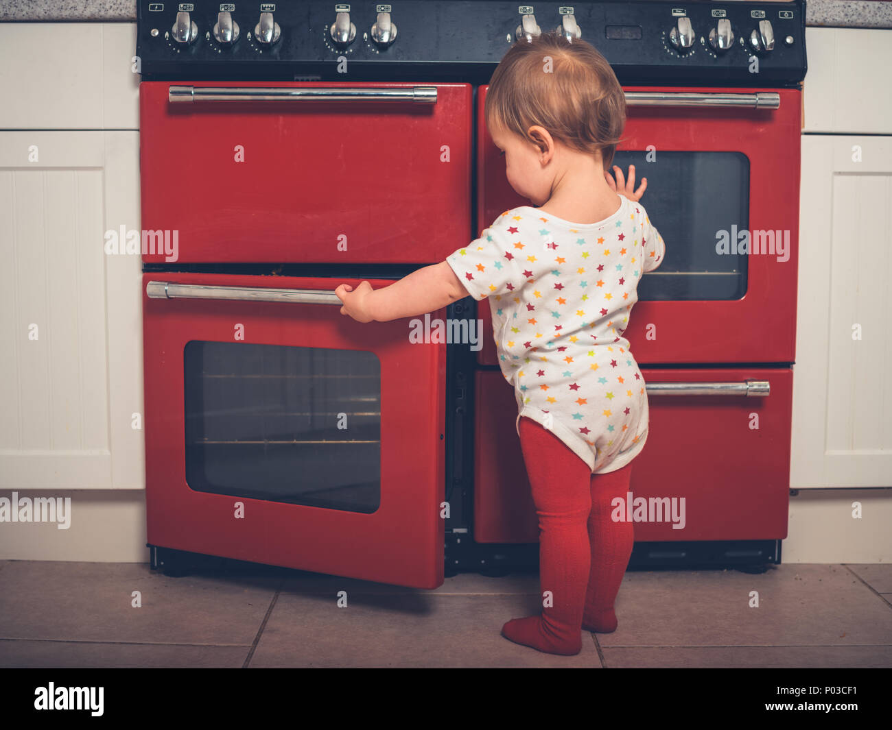 A cute little boy is in the kitchen opening the oven Stock Photo - Alamy