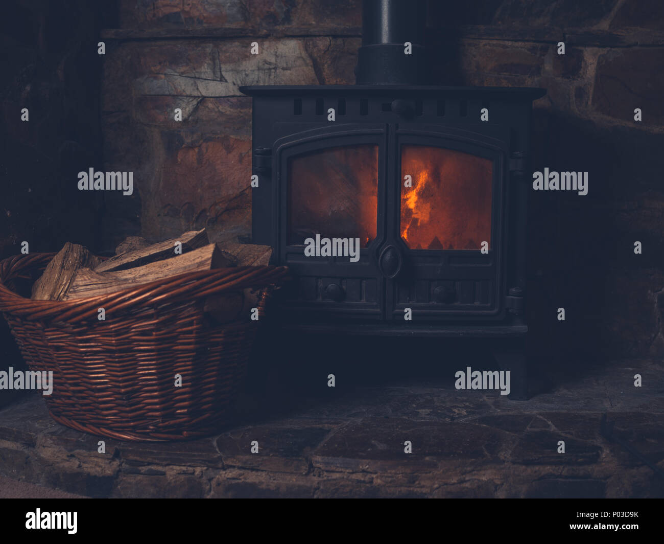 A traditional log burner with a basket of firewood and a lit fire Stock ...
