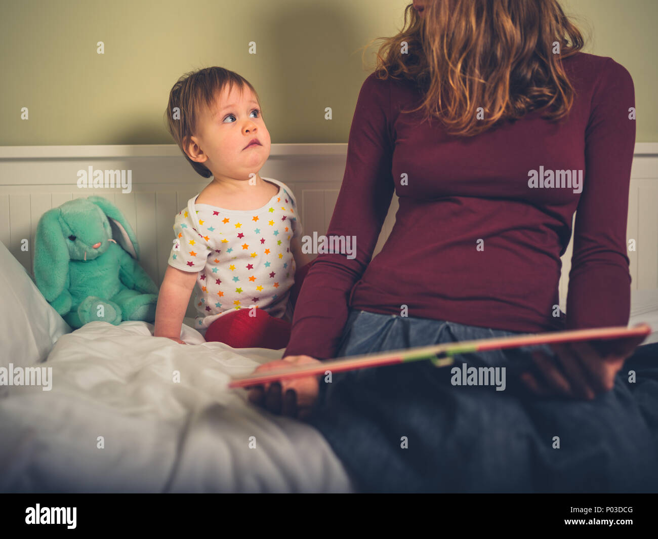 A little boy is being read to by his mother and is looking at her ...