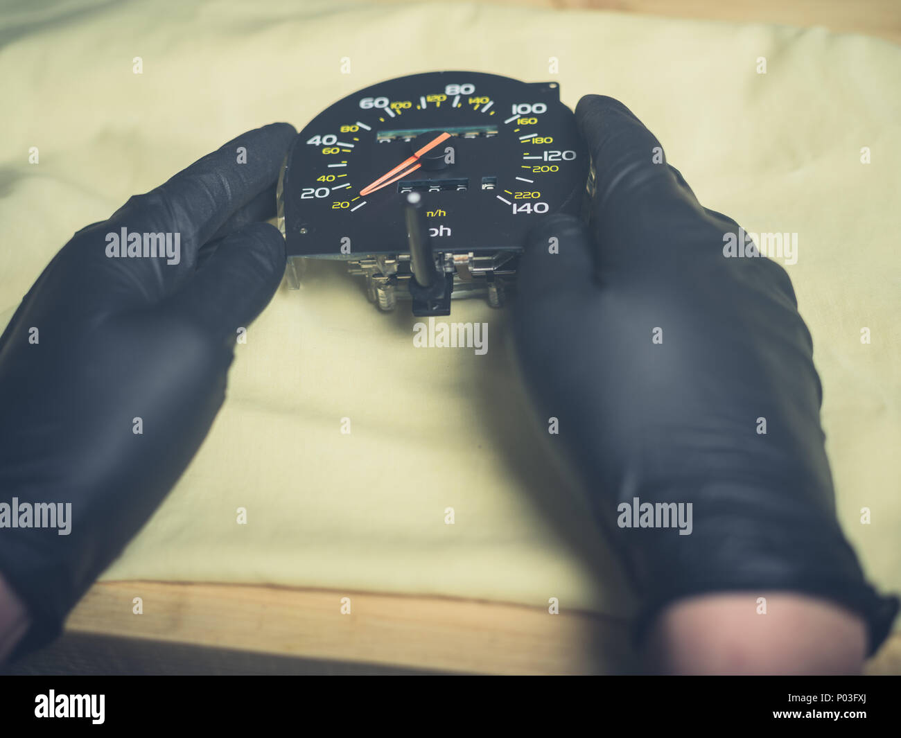 The gloved hands of a man holding a speedometer and odometer at a table ...