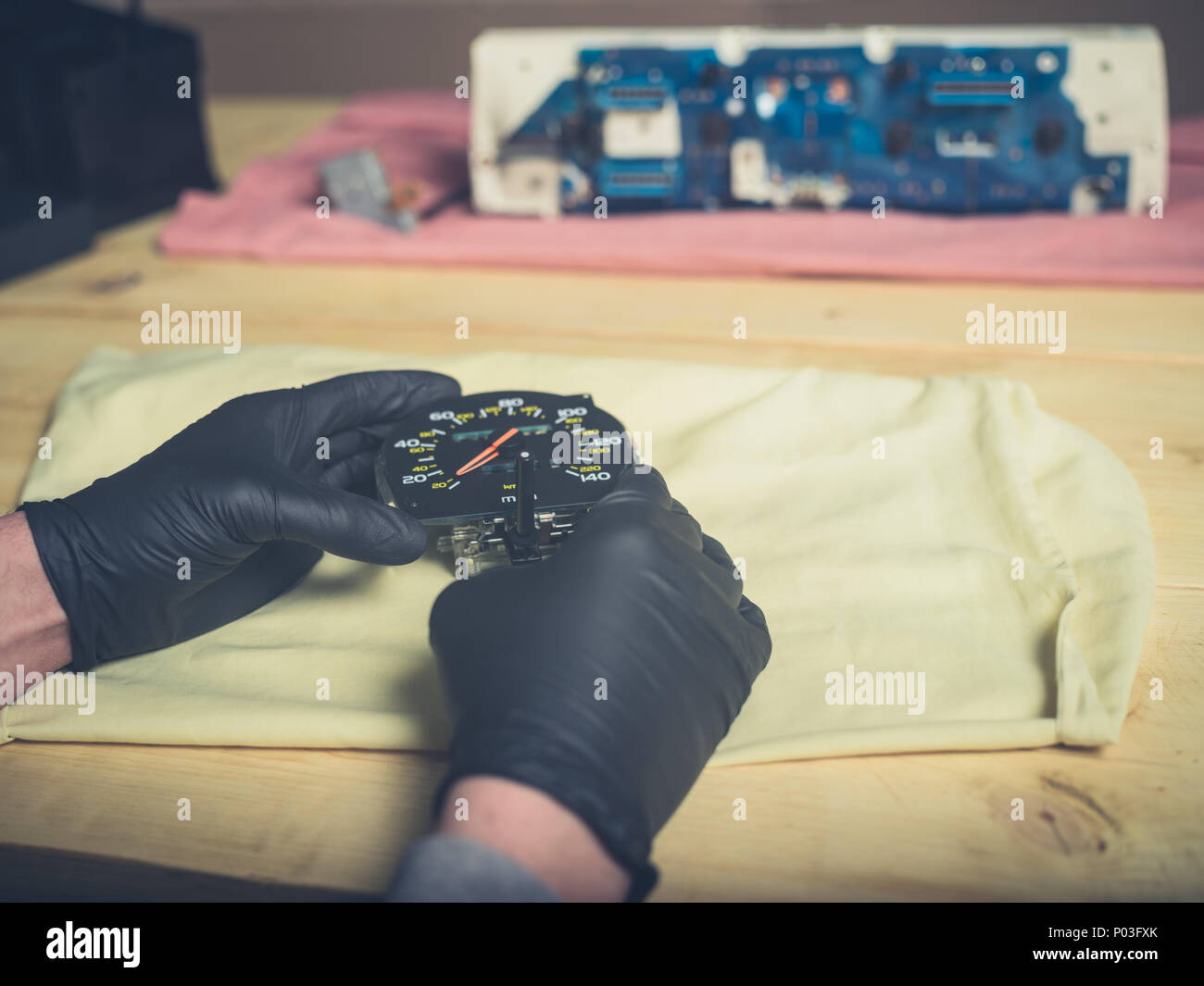 The gloved hands of a man holding a speedometer and odometer at a table ...
