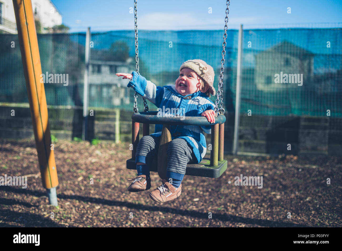 A happy little boy is swinging on a swing in a playground Stock Photo ...