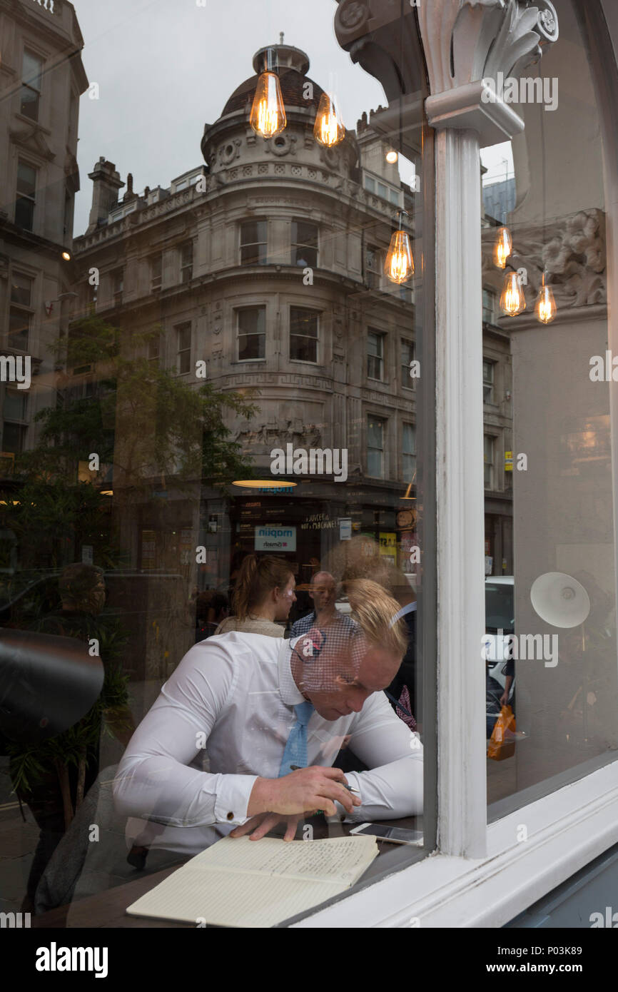 A young man concentrates on writing in a notebook in the window of a ...