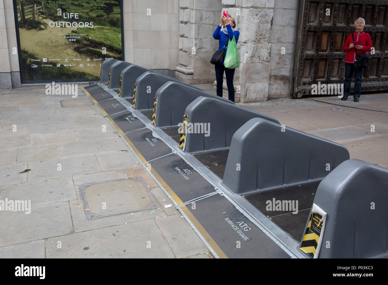Pedestrians walk over security barriers at one of the entrances to ...